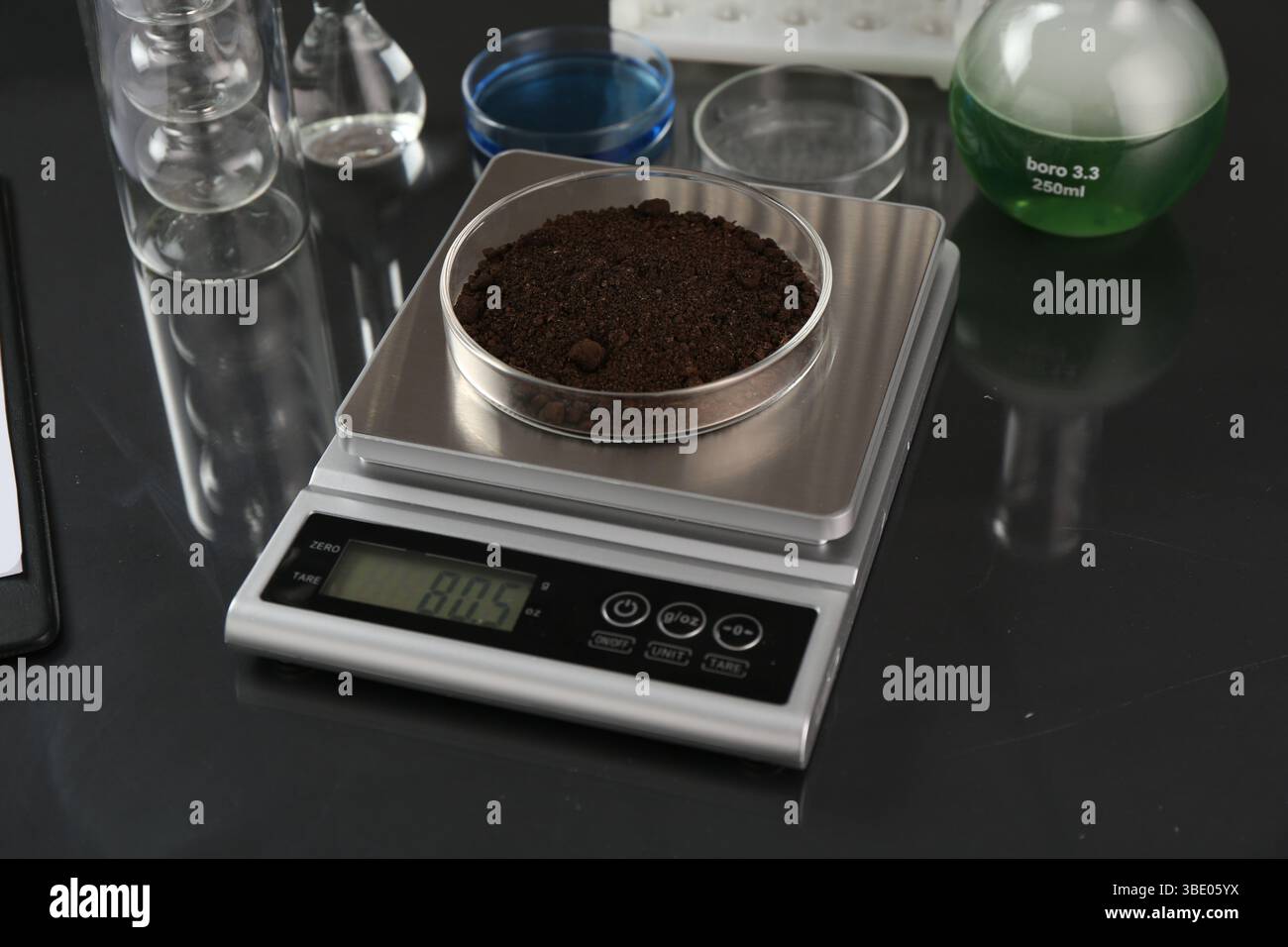 Scale with Petri dish of sample and other laboratory glassware on black ...