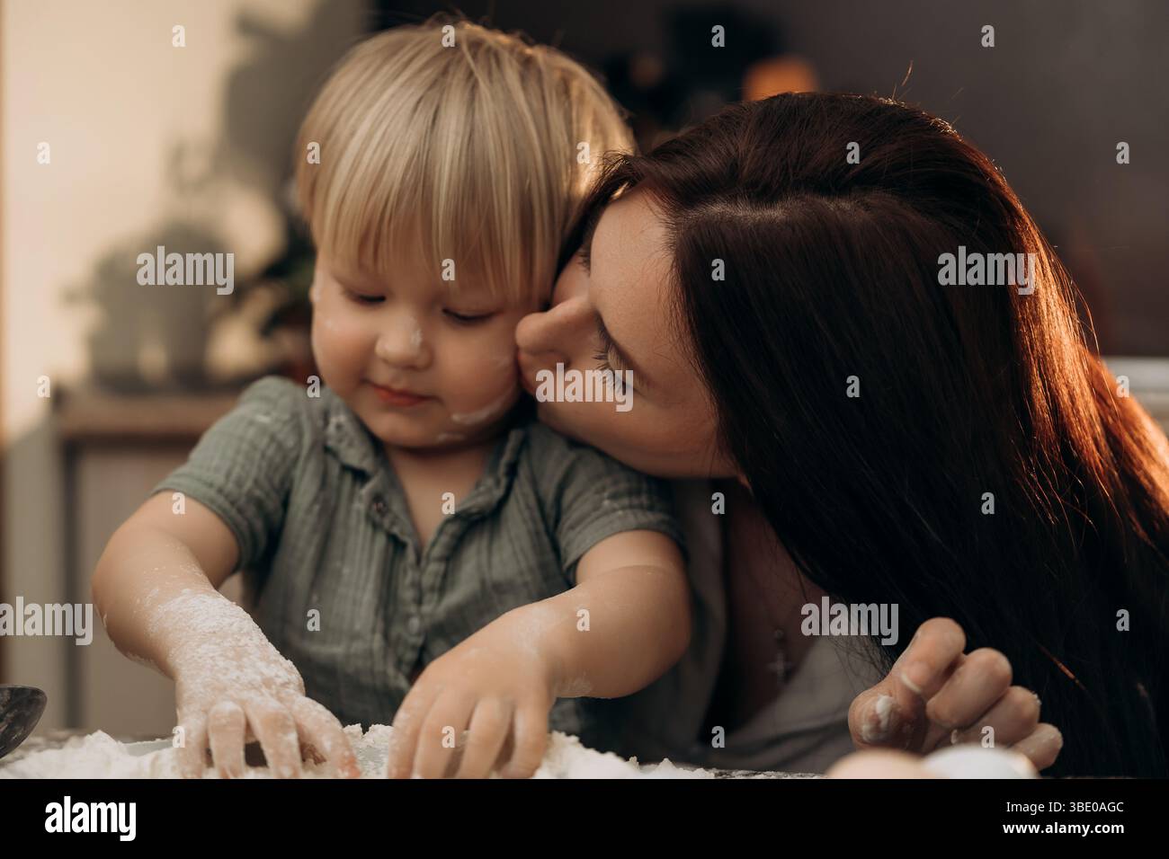 Tender kiss on flour dusted cheek as toddler explores kitchen textures capturing authentic ...