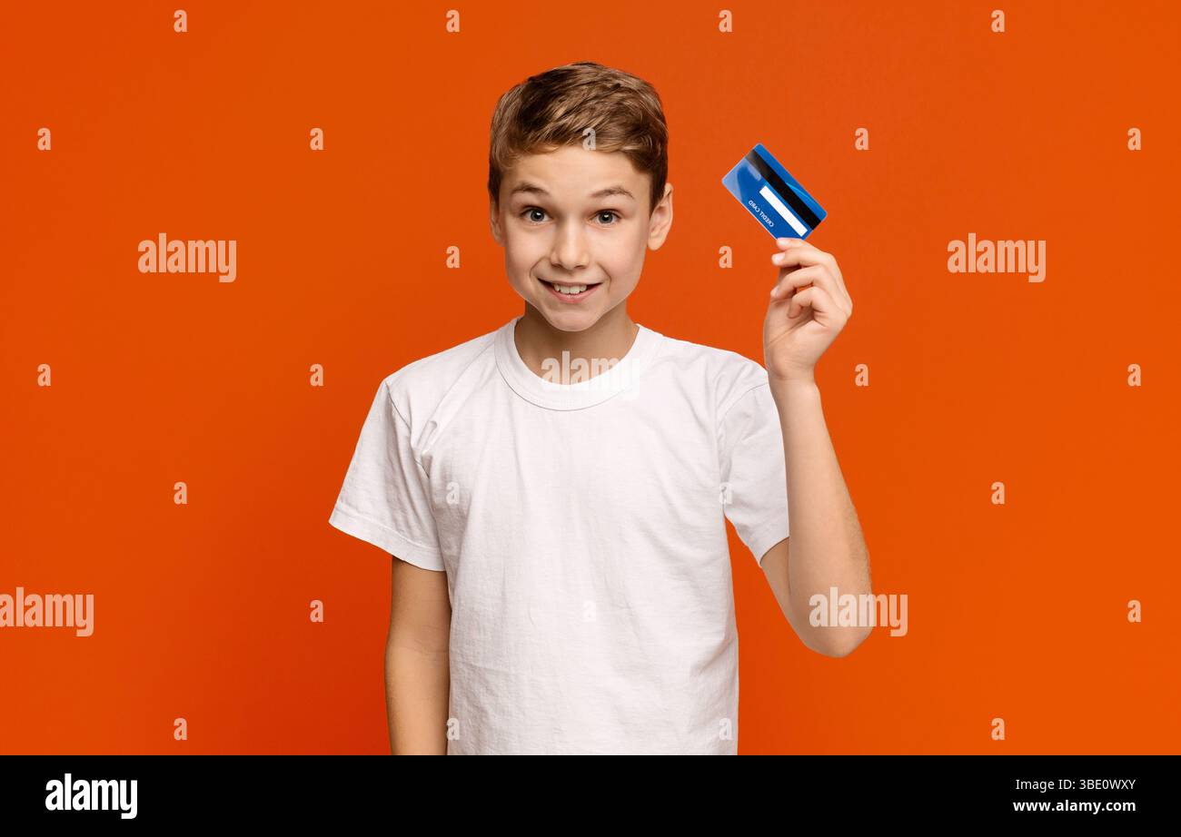 Cute boy holding credit card, orange studio background Stock Photo - Alamy