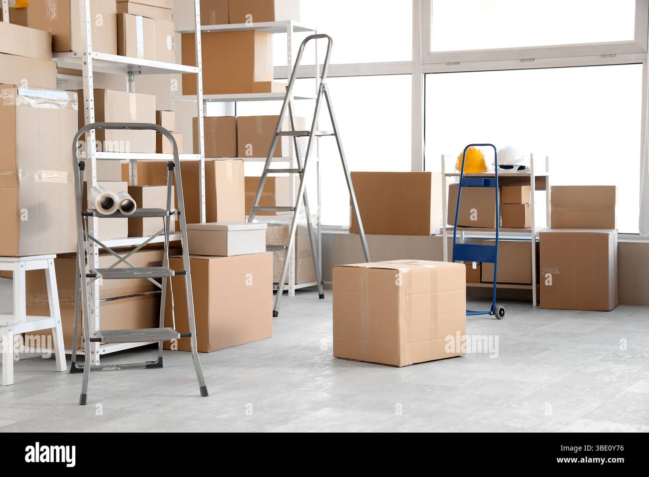 Interior of warehouse with shelf units, cardboard boxes and stepladders ...