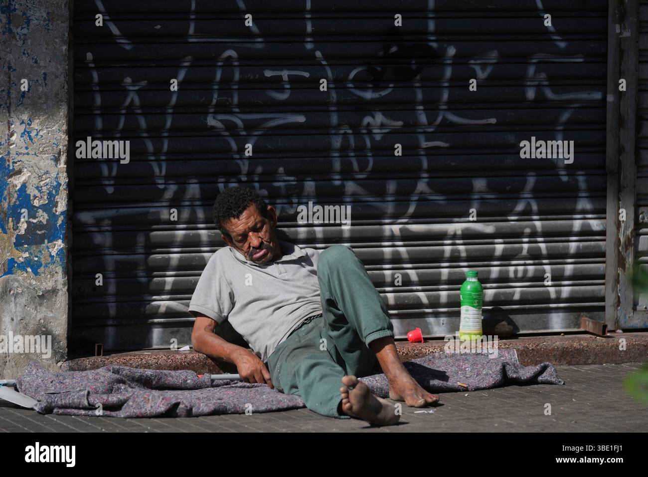 A homeless man sleeps on the sidewalk in a downtown area popularly ...