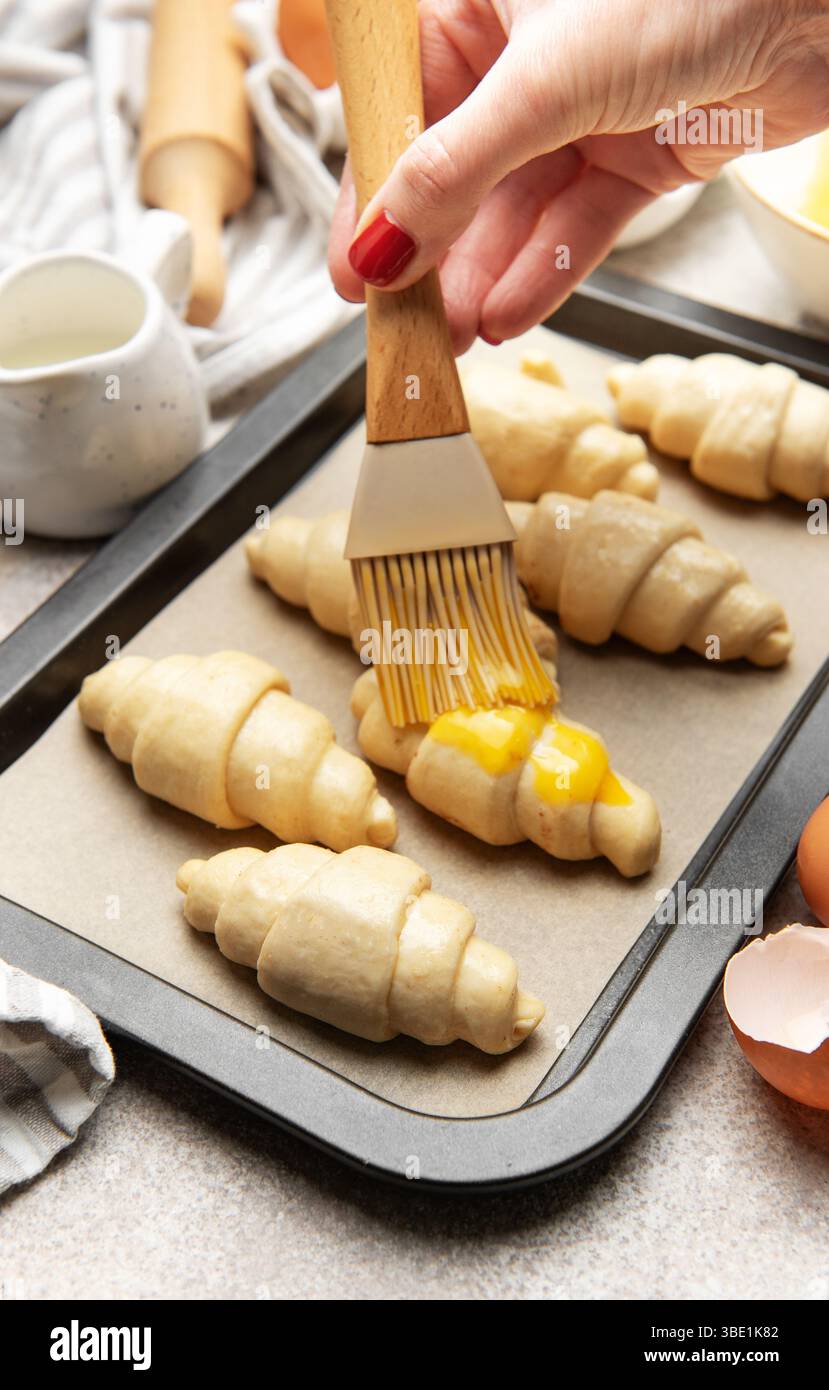 Baker glazing croissants with egg yolk before baking, adding a golden ...