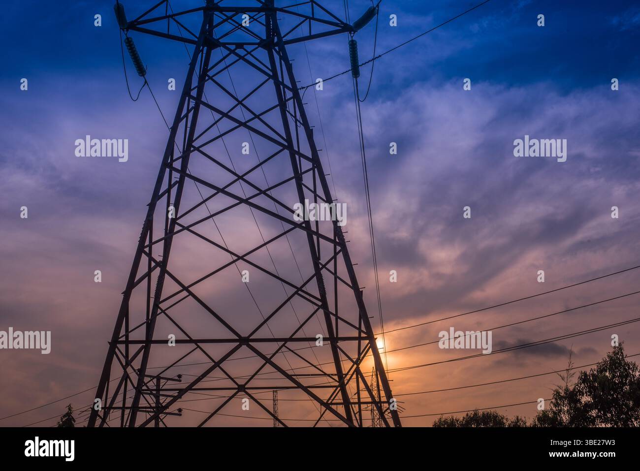 A tall steel high-voltage transmission tower stands against a blue sky ...