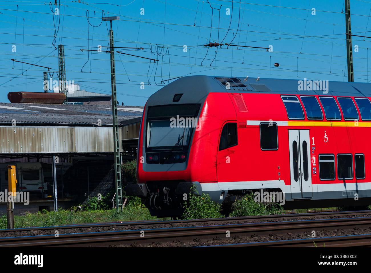 A modern red train approaches a station under a bright blue sky ...