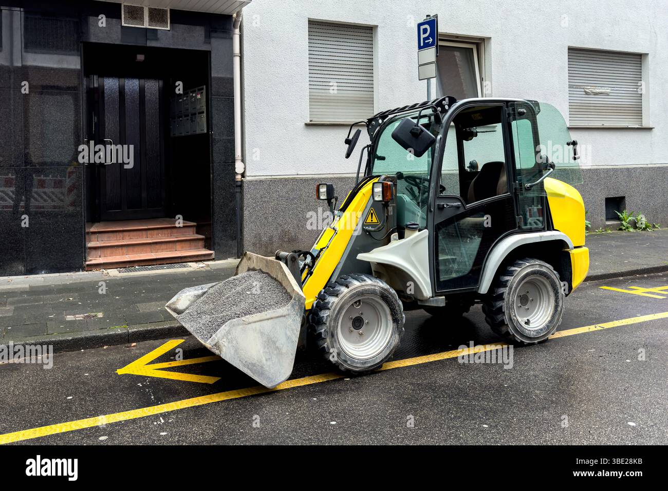 A small construction vehicle with a front loader is parked on a city ...