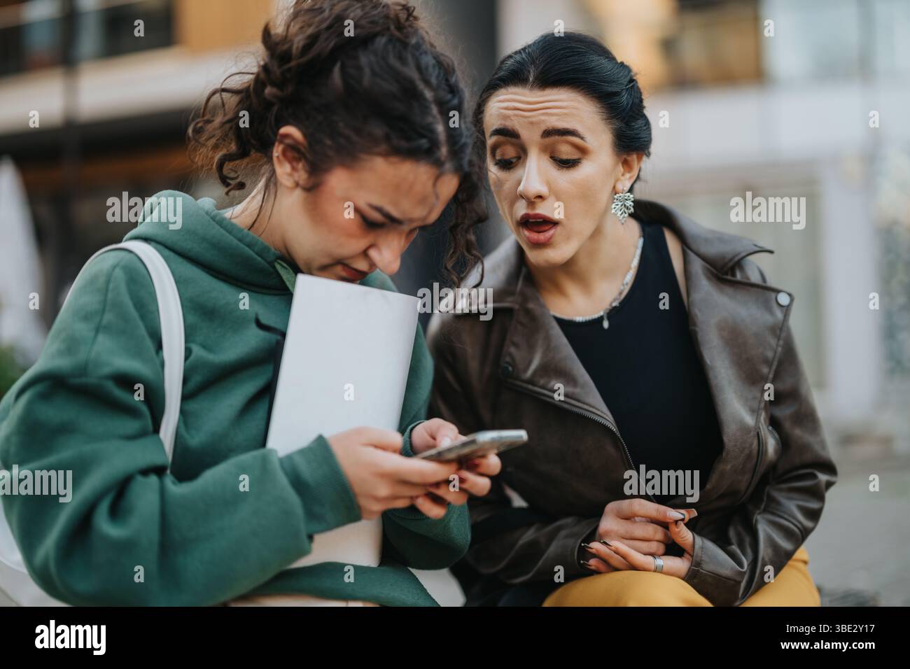 Two women sharing intense expressions while discussing over a mobile ...