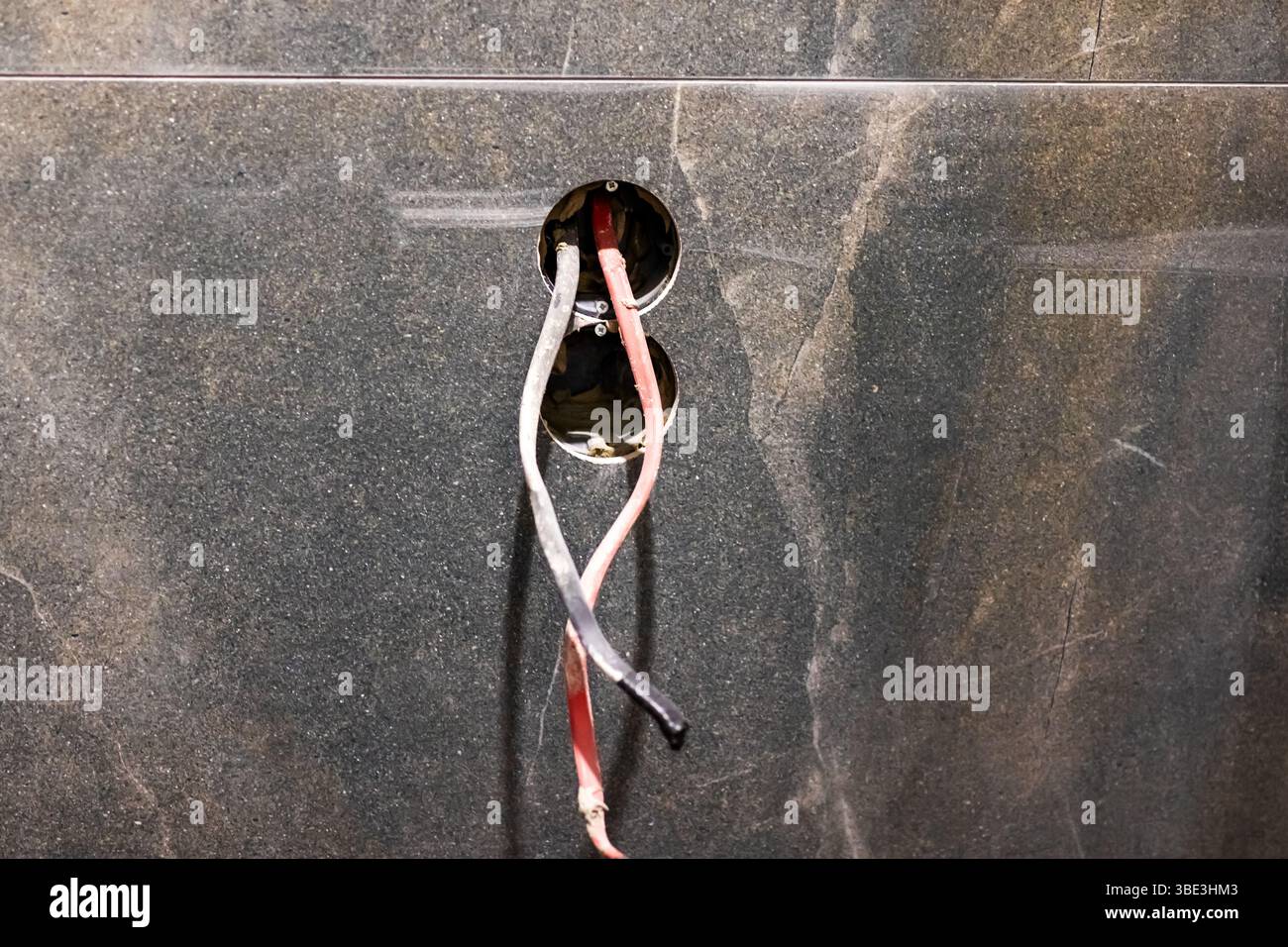 A myriad of wires is dangling from an opening in the wall, creating an interesting, yet somewhat ...