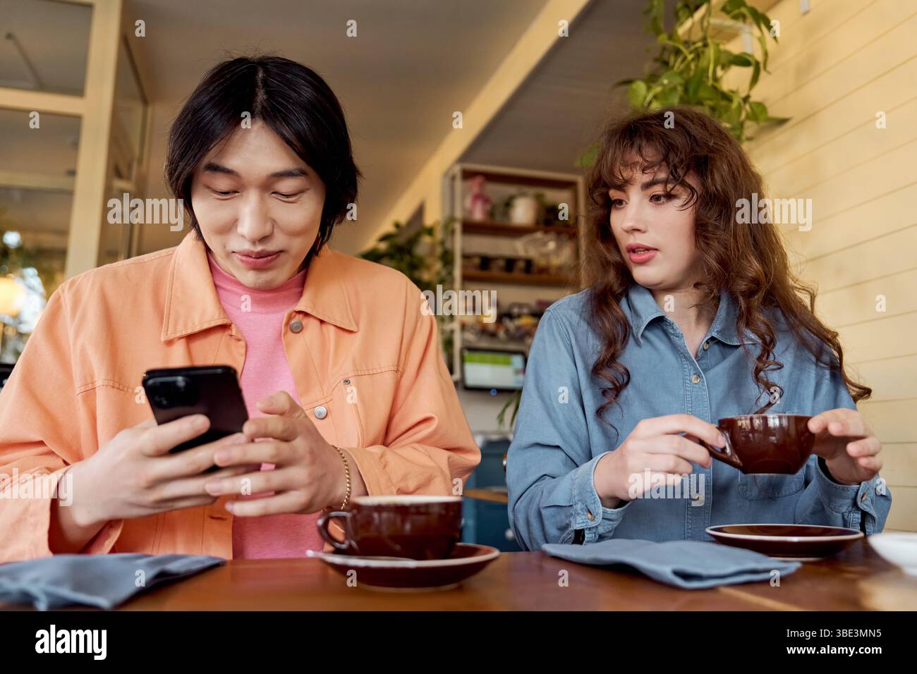 A young asian man shows something amusing to his friend in a warm cafe ...