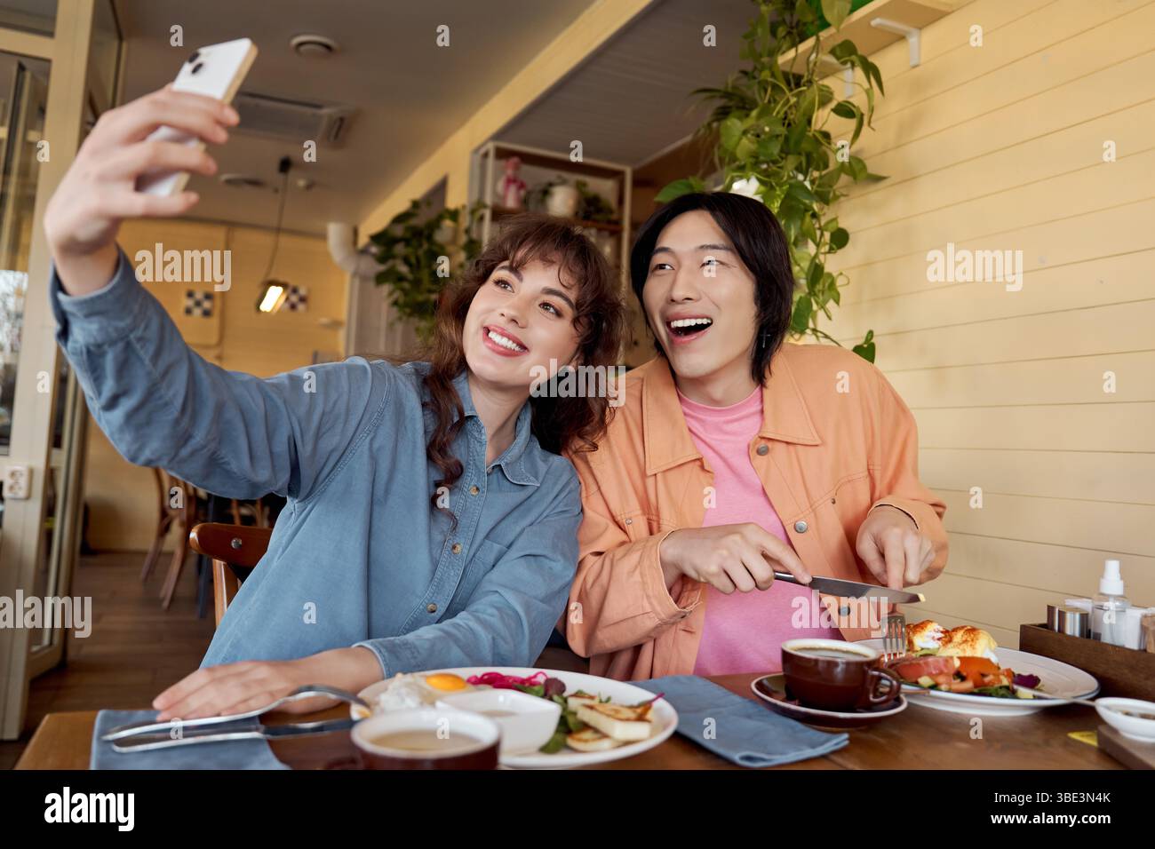Two multicultural friends enjoy a lighthearted brunch while taking ...