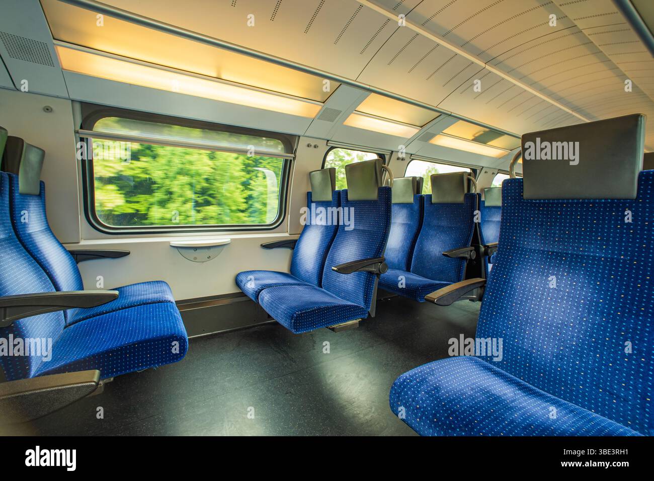 Empty blue cloth seats inside passenger train in Europe. Large window side seats, moving train ...