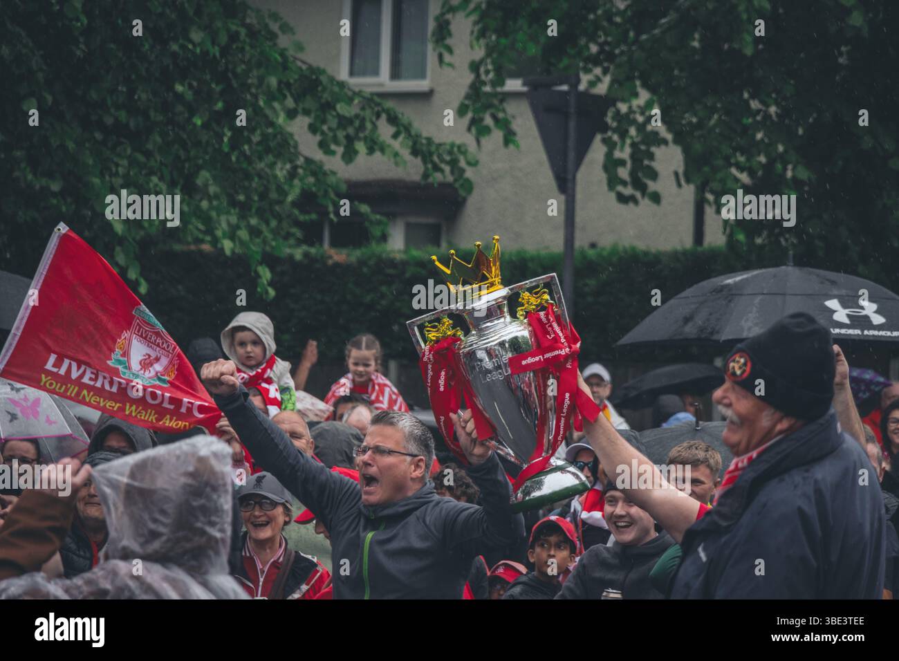 Male Liverpool supporters waving a replica Premier League trophy in a ...