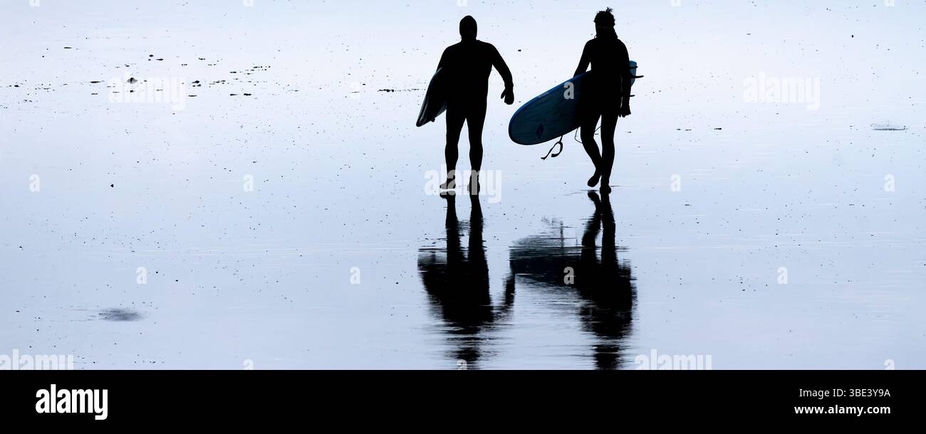 A panoramic image of two surfers seen in silhouette walking home after ...