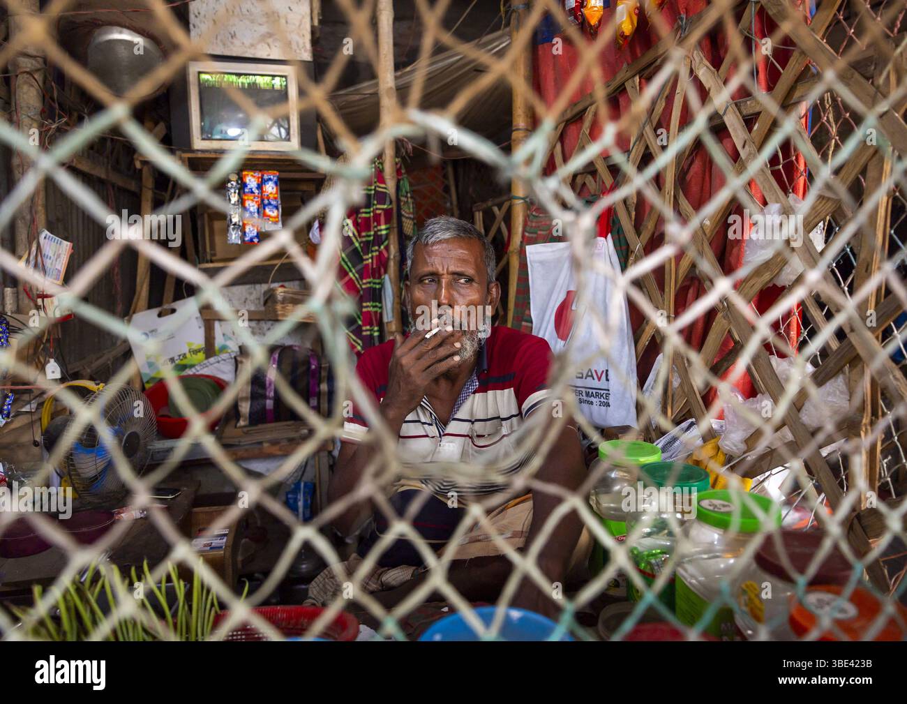 Vendor smoking in a shop protected by a net, Dhaka Division, Dhaka ...