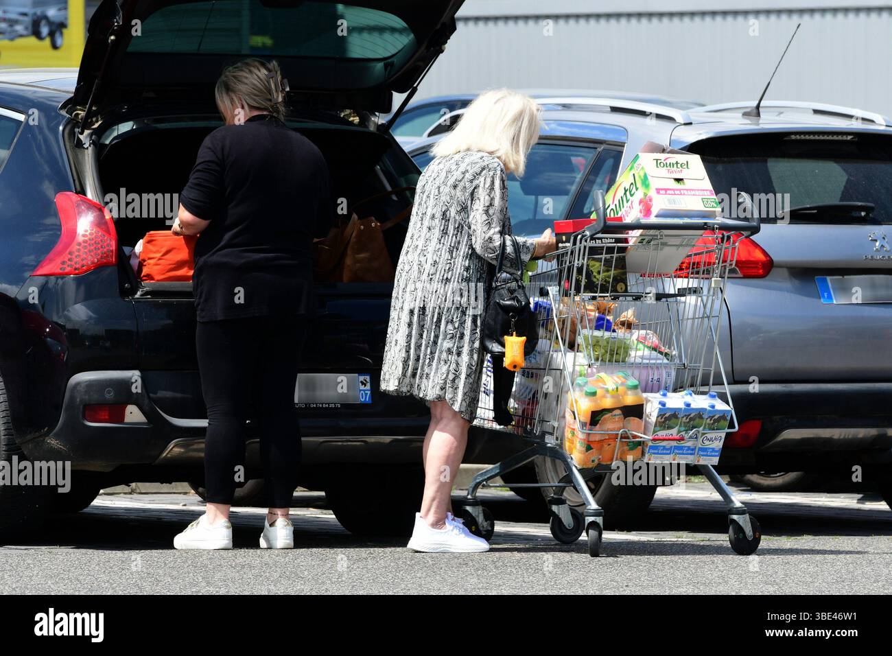 Two women next to cars seen with a shopping cart of groceries outside ...