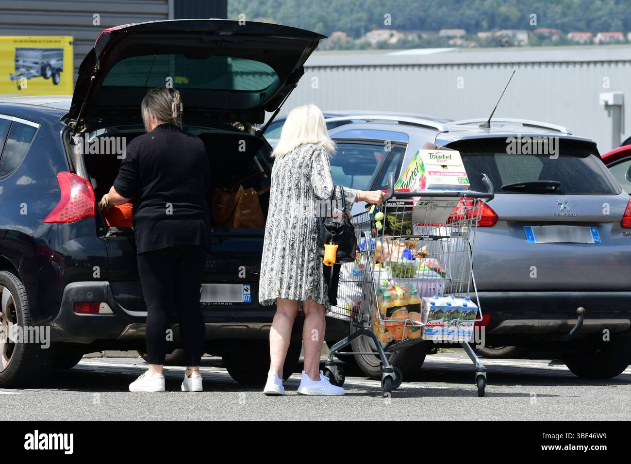 Two women next to cars seen with a shopping cart of groceries outside ...