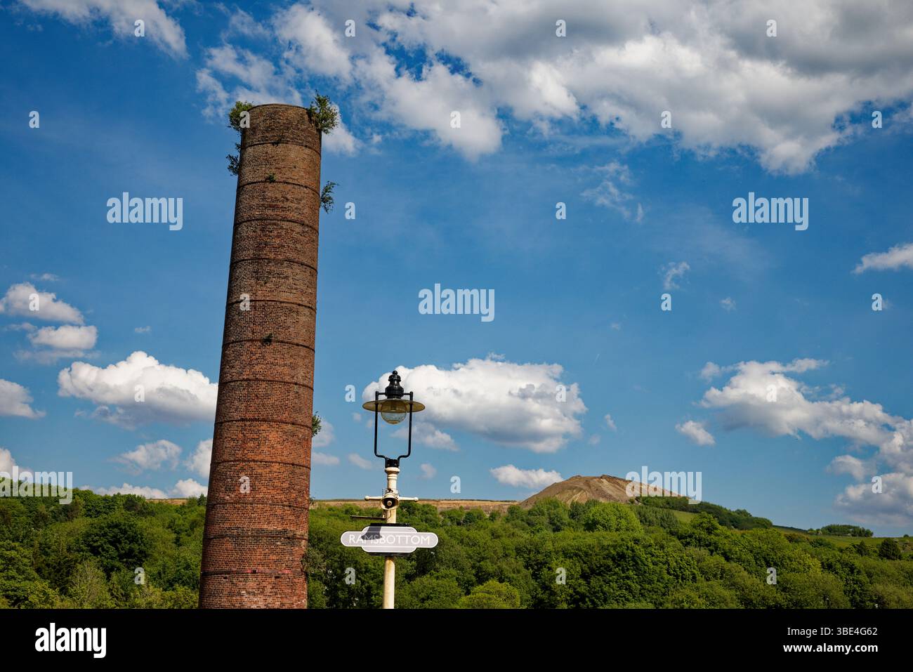 A brick Victorian chimney of an abandoned mill with a wooded hillside ...
