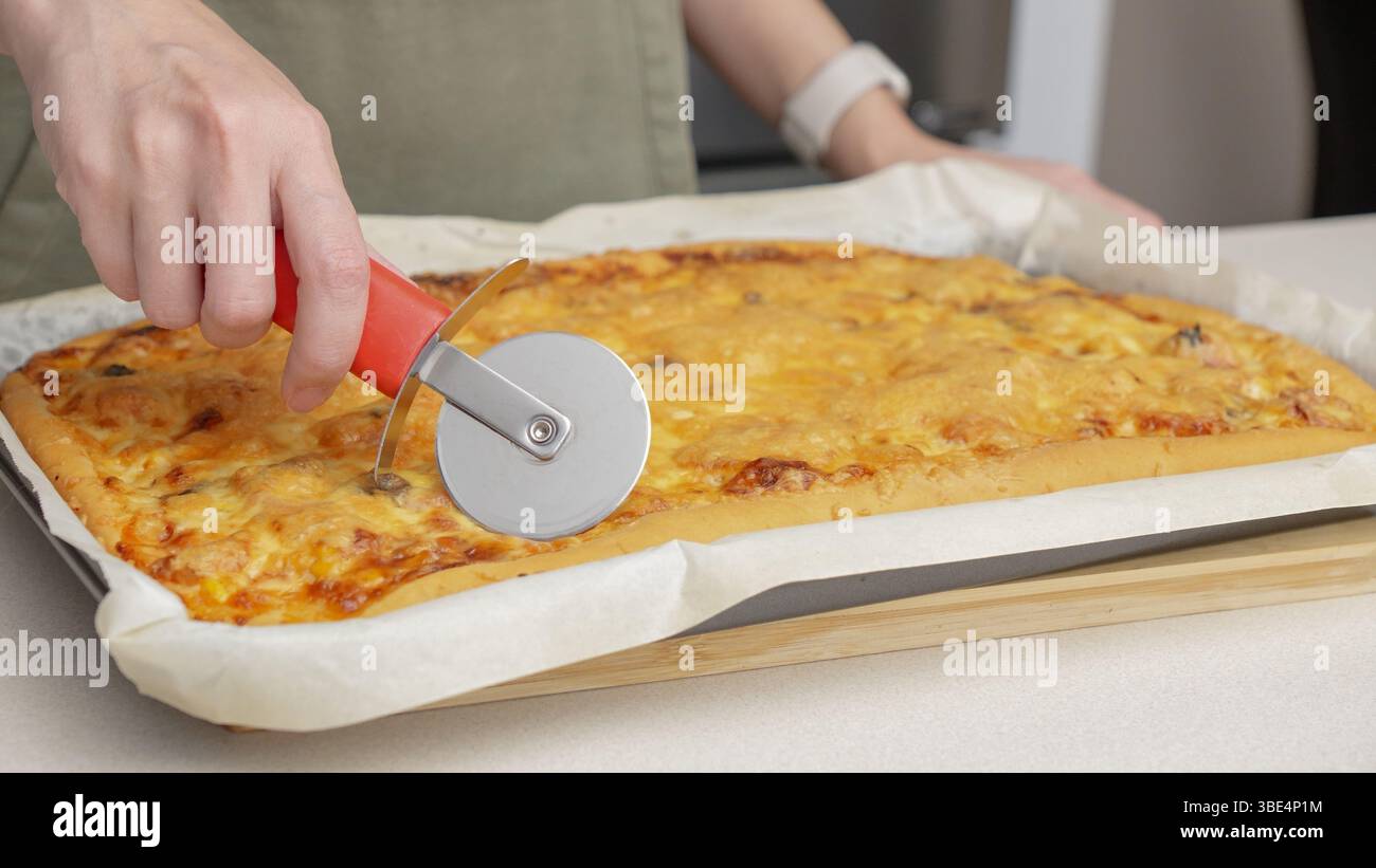 Cutting pizza with a round cutter knife. Close-up of delicious pizza ...