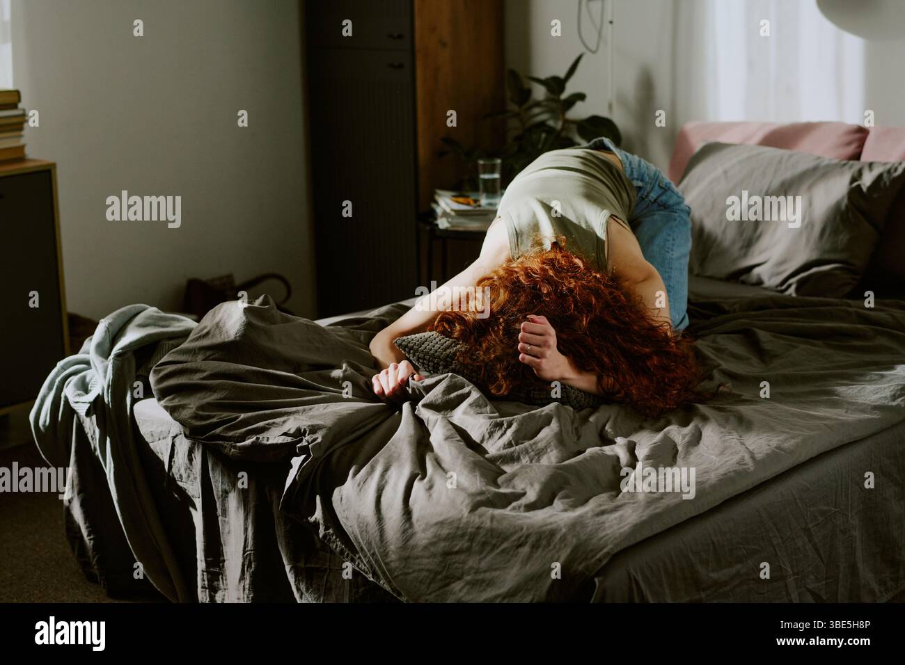 Woman with red hair bent over bed in cozy room with natural light ...