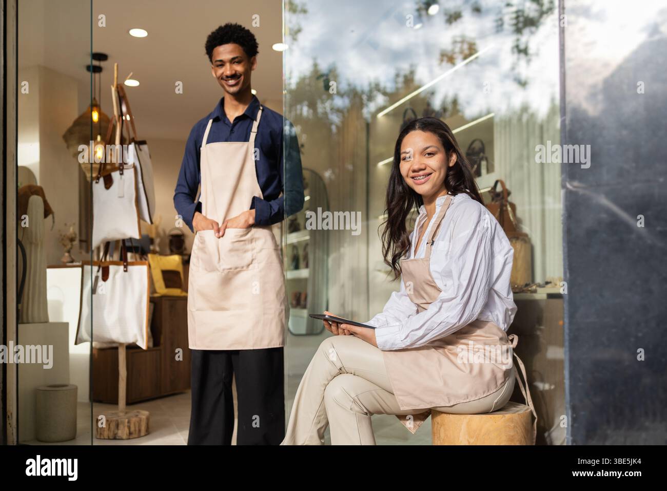 Two smiling shop assistants in a chic bag store, both wearing aprons ...