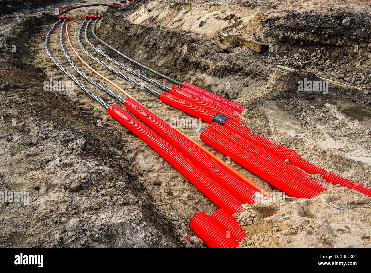 Laying a new underground high-voltage power cable in red corrugated ...