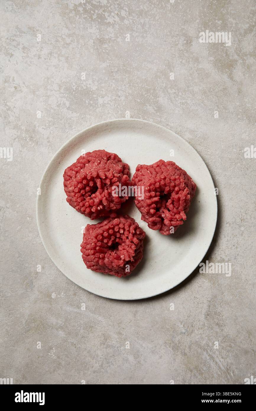 Three mounds of freshly ground beef presented on a white ceramic plate ...