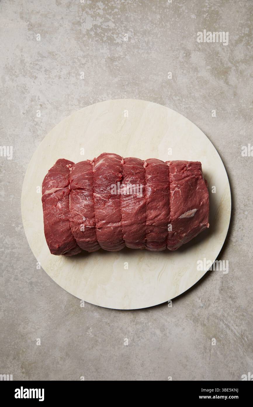 A raw beef roast, expertly tied and ready for cooking, sits on a rustic ...