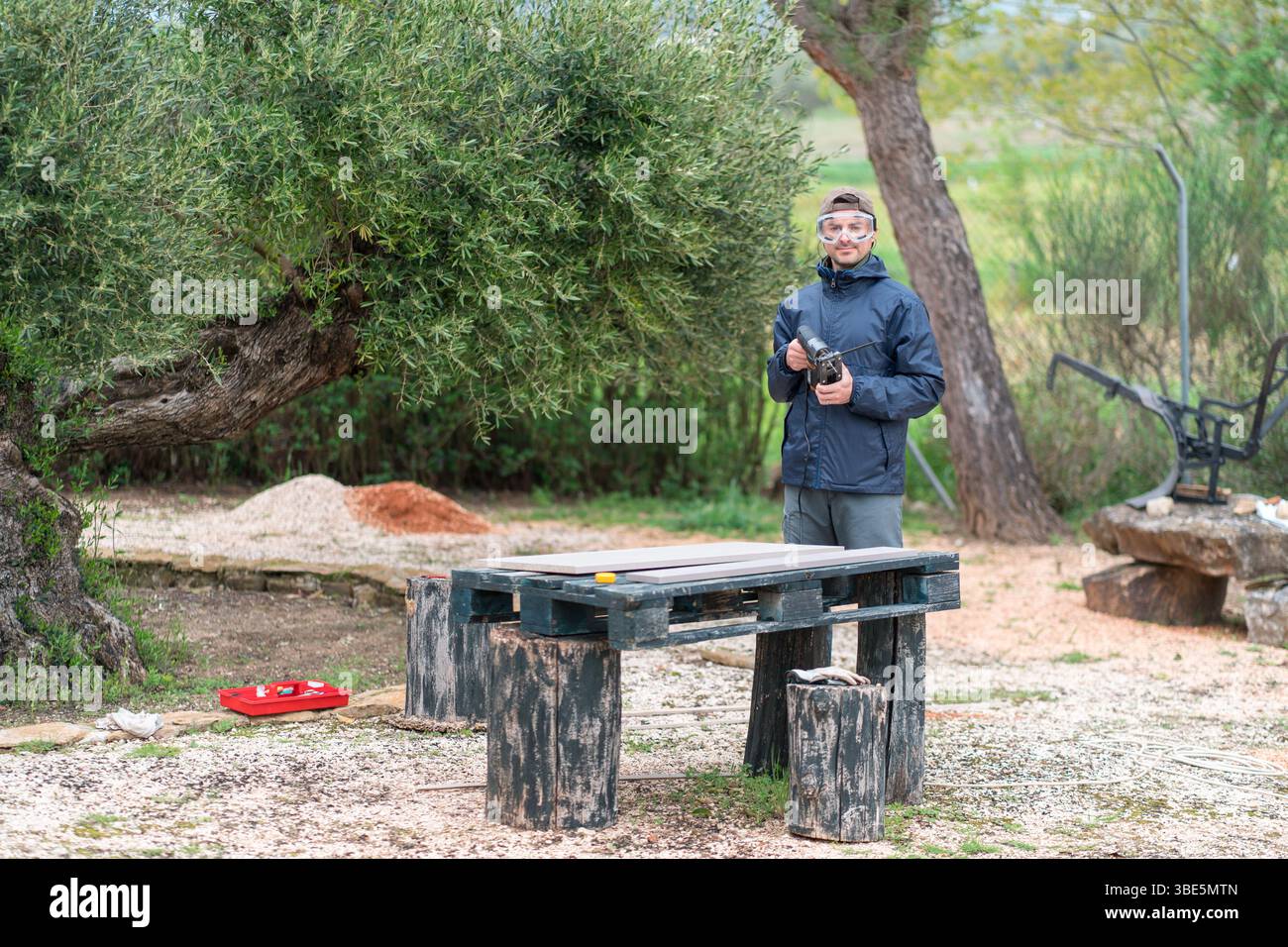 A man is pictured outdoors engaging in a carpentry activity, surrounded ...