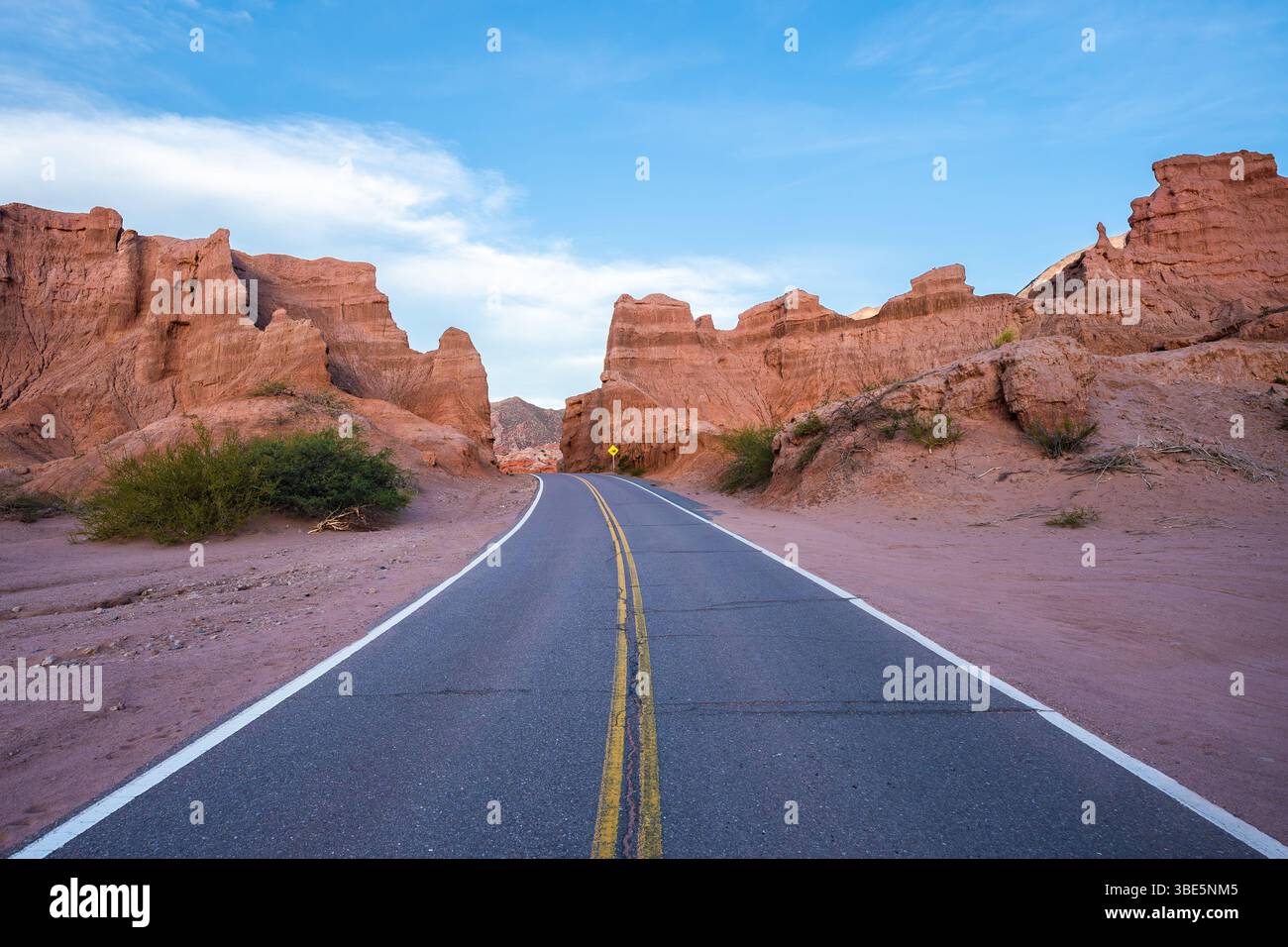 A scenic road curves between dramatic red rock formations under a clear ...