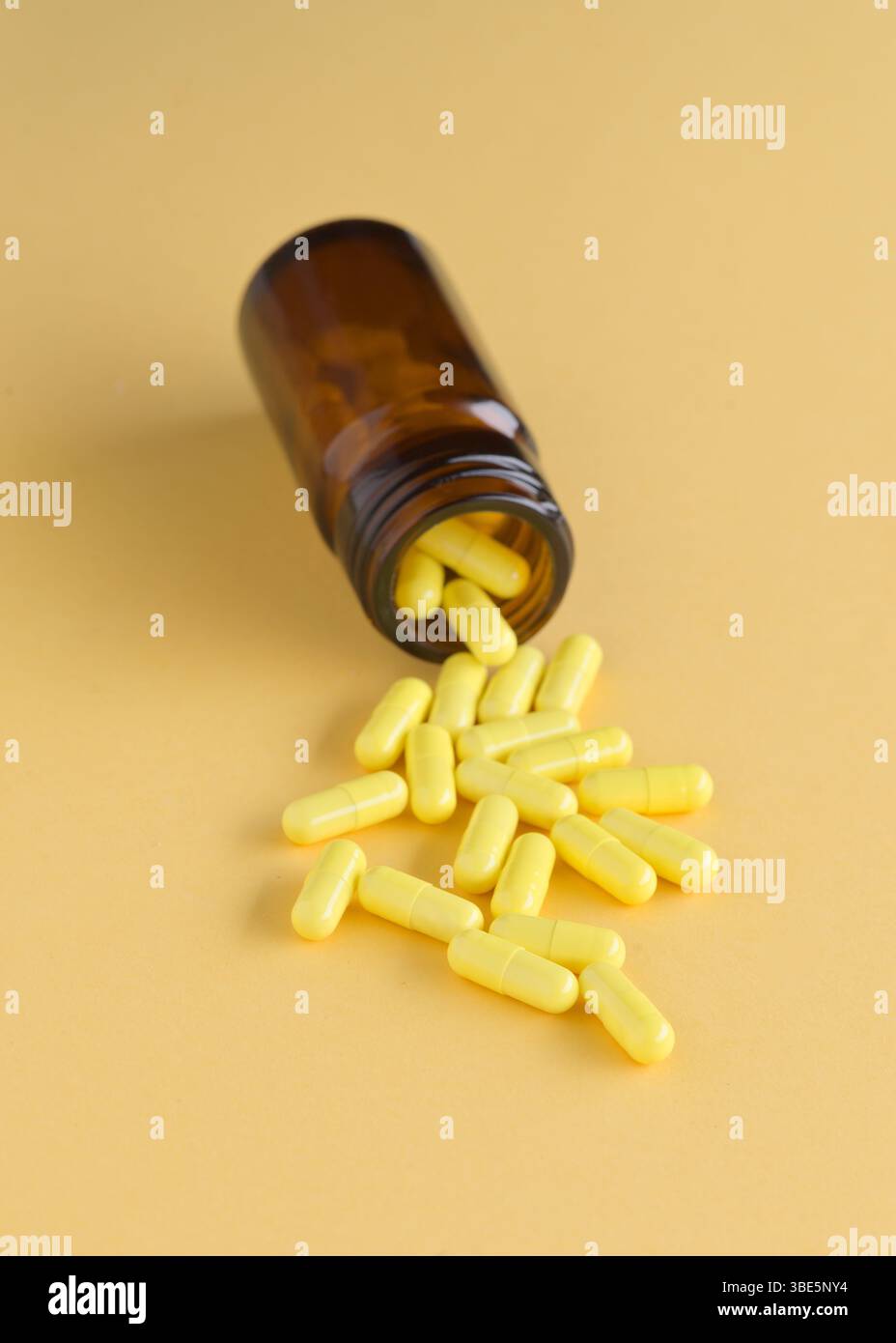 Close up of yellow capsules spilled from a brown bottle on a smooth ...