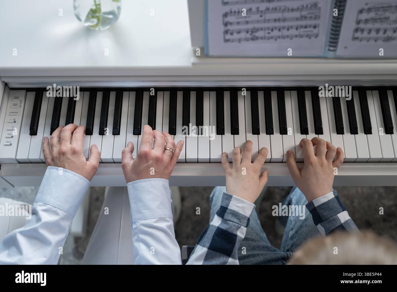 Close-up view of adult and child hands playing the piano together, emphasizing learning and ...