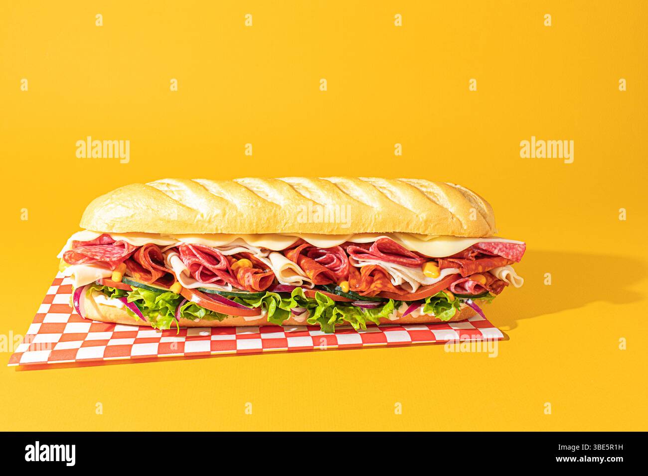 A delicious, fully loaded submarine sandwich rests atop a red and white ...