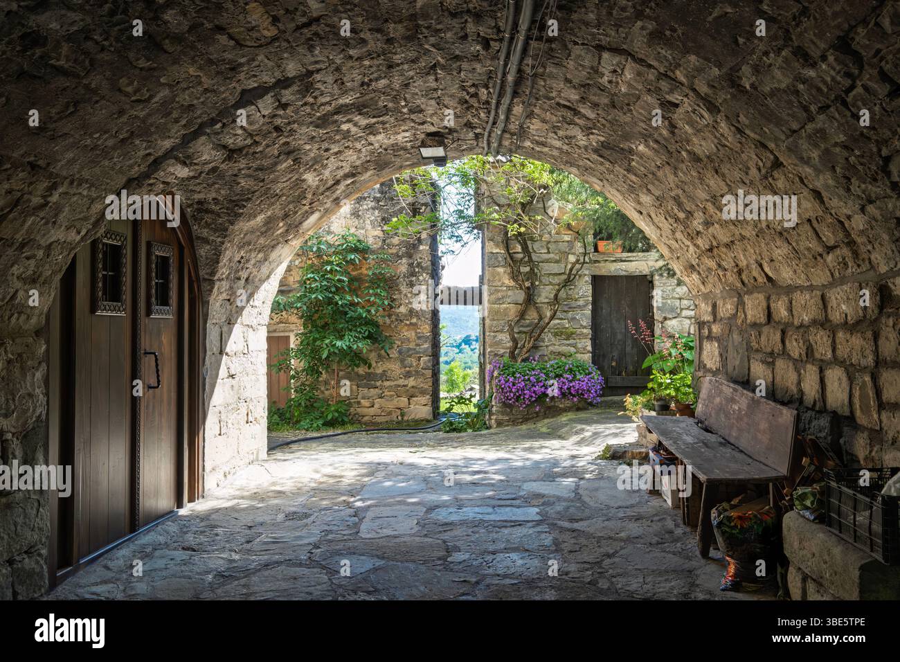 An ancient stone archway frames a rustic courtyard in a traditional ...