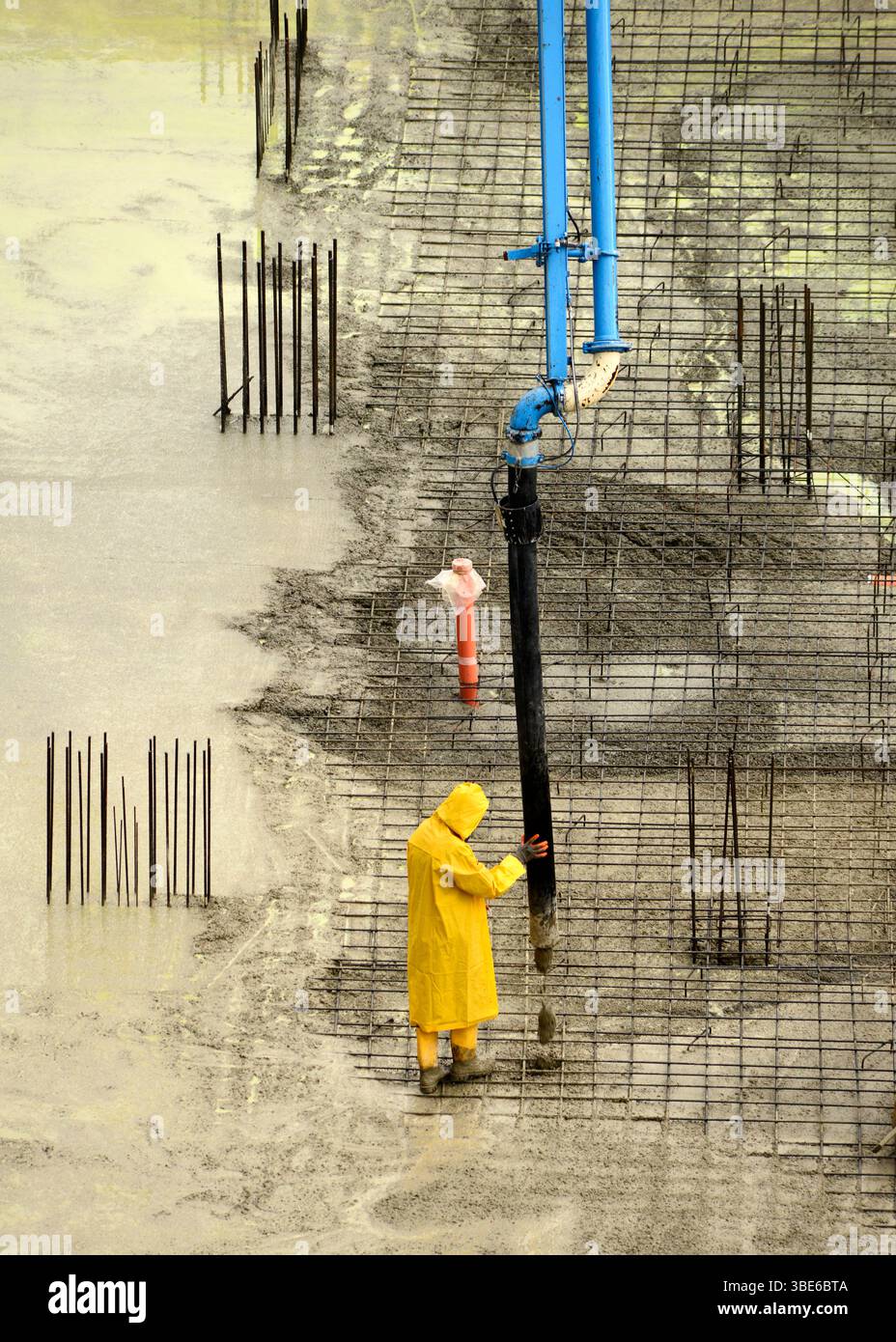 Construction worker in yellow waterproof poncho pouring concrete from a ...