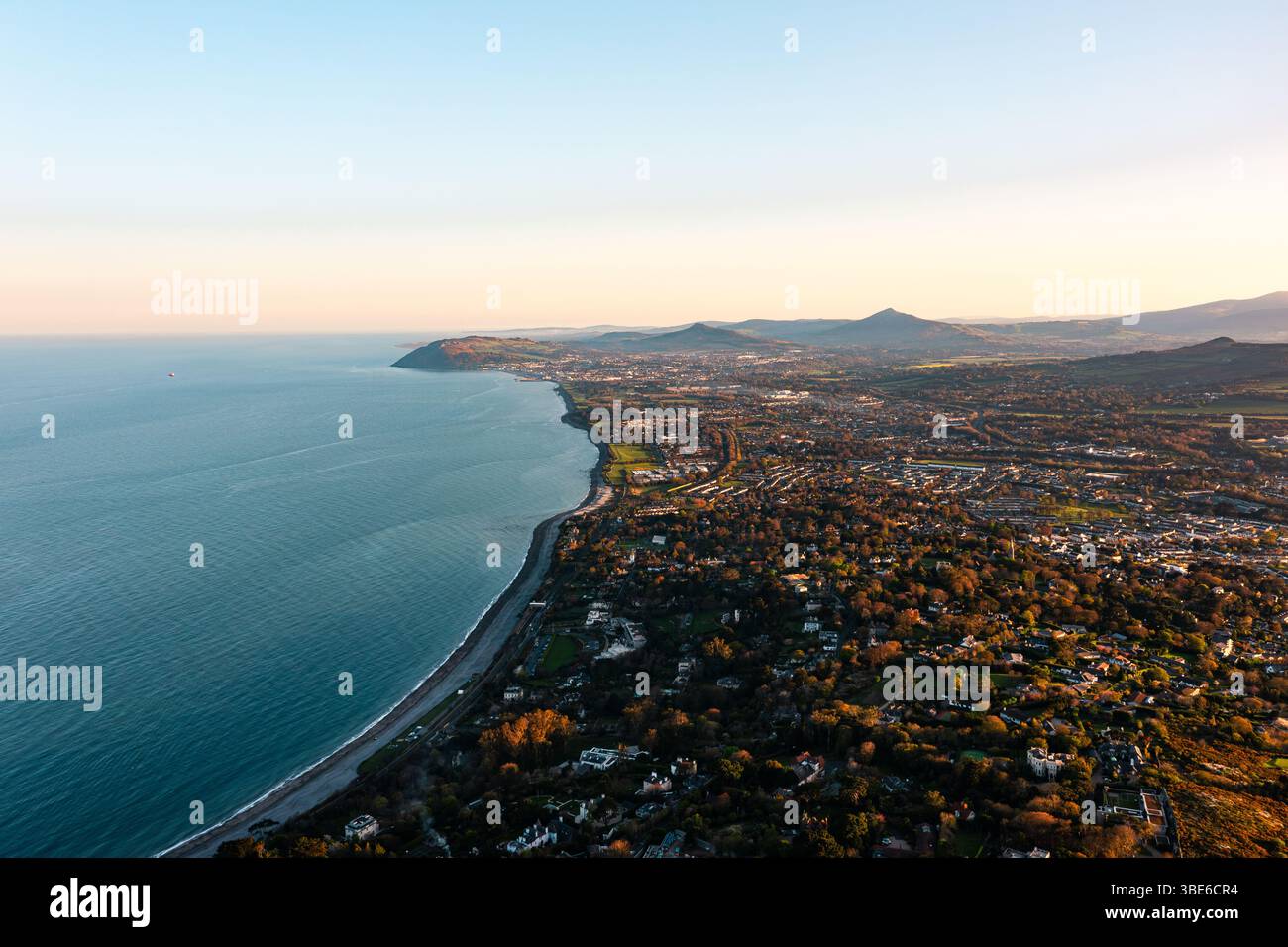 Aerial view of Killiney Strand with calm sea, mountain silhouette, and ...