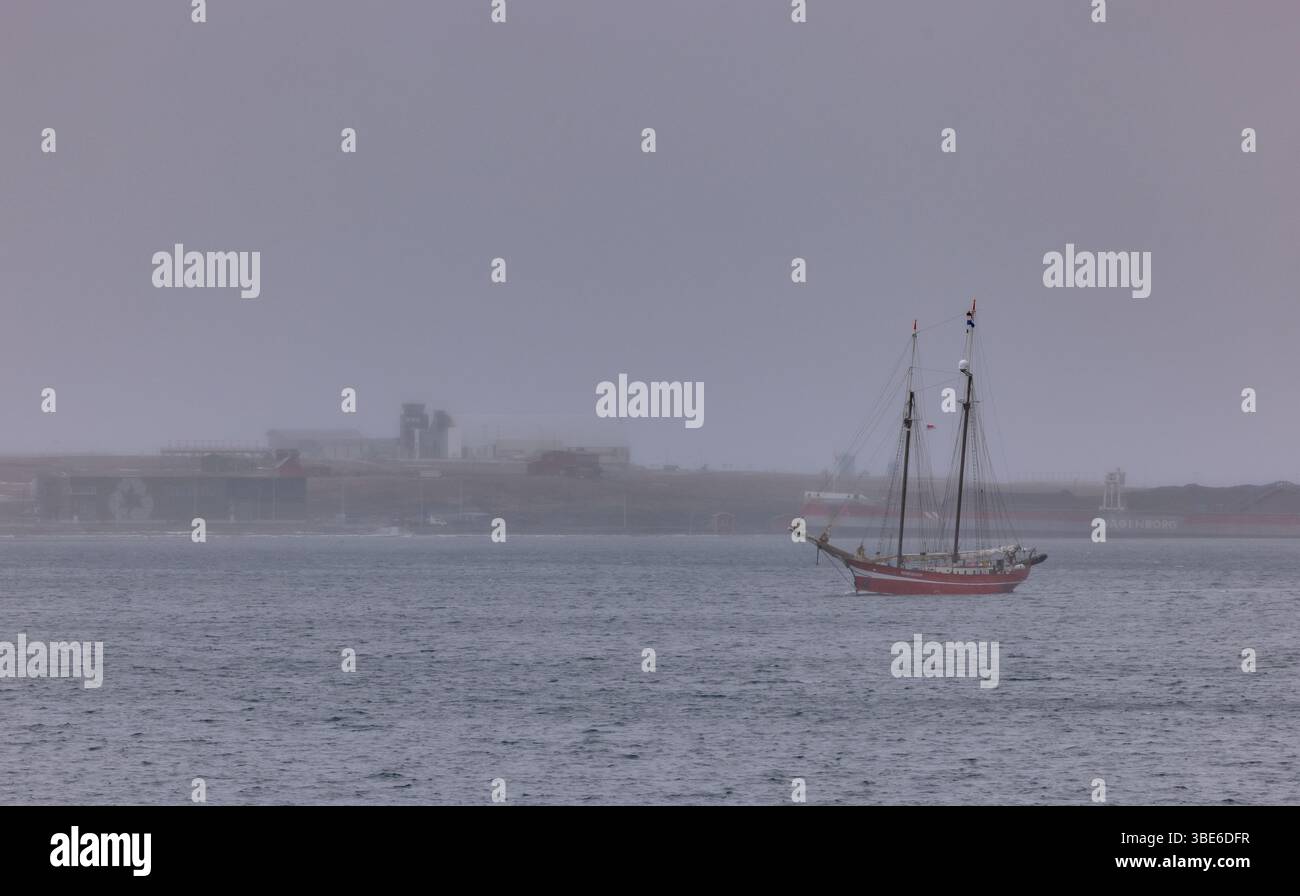 Classic sailing ship underway in the mist near the industrial coastline ...