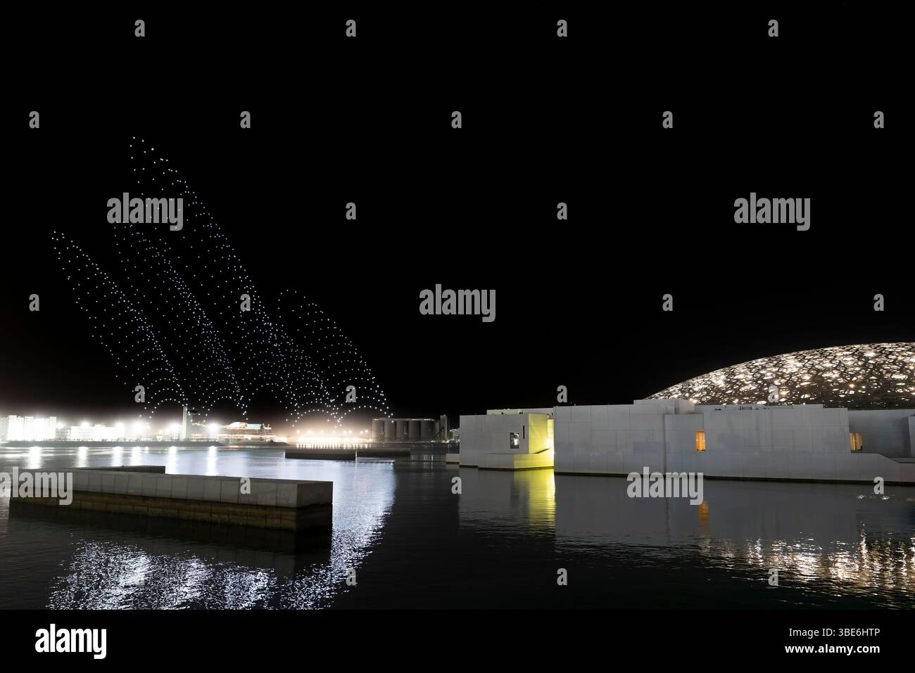 A series of drone lights create an arc above the illuminated Louvre Abu ...