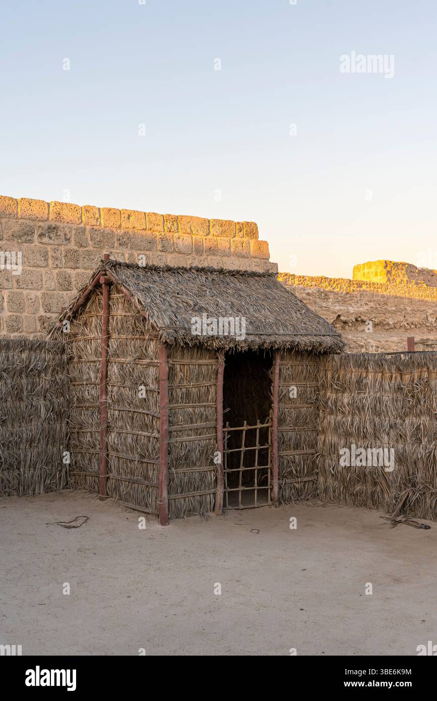 Thatched shelter stands beside stone ruins in the sandy grounds of ...