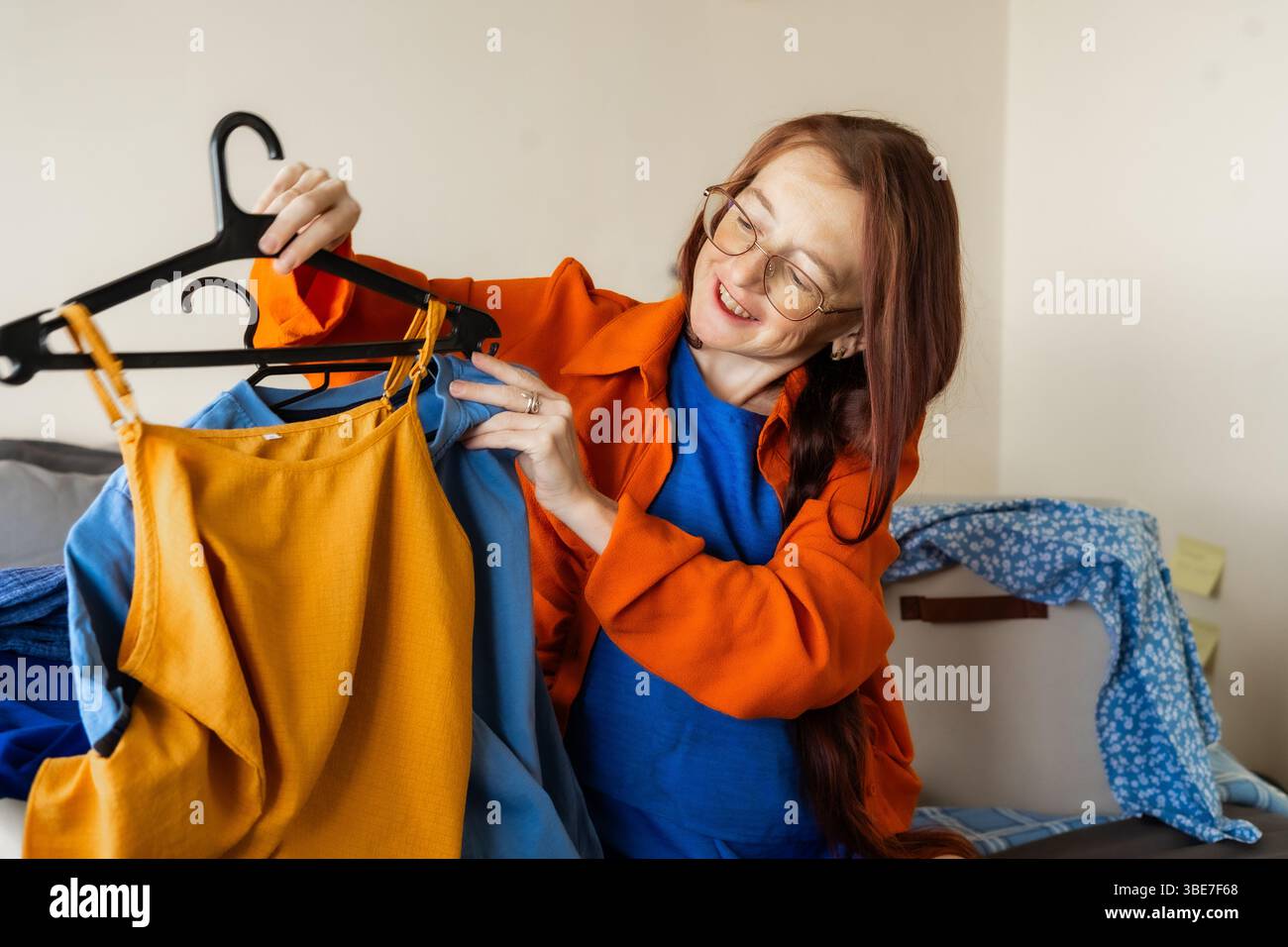 Woman selecting bright clothes for a capsule wardrobe while smiling and ...