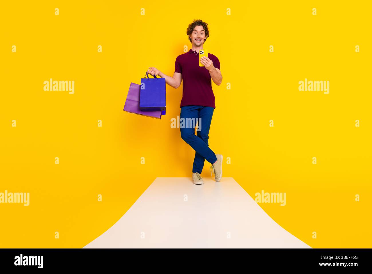 Joyful man with shopping bags and smartphone stands on vibrant yellow ...