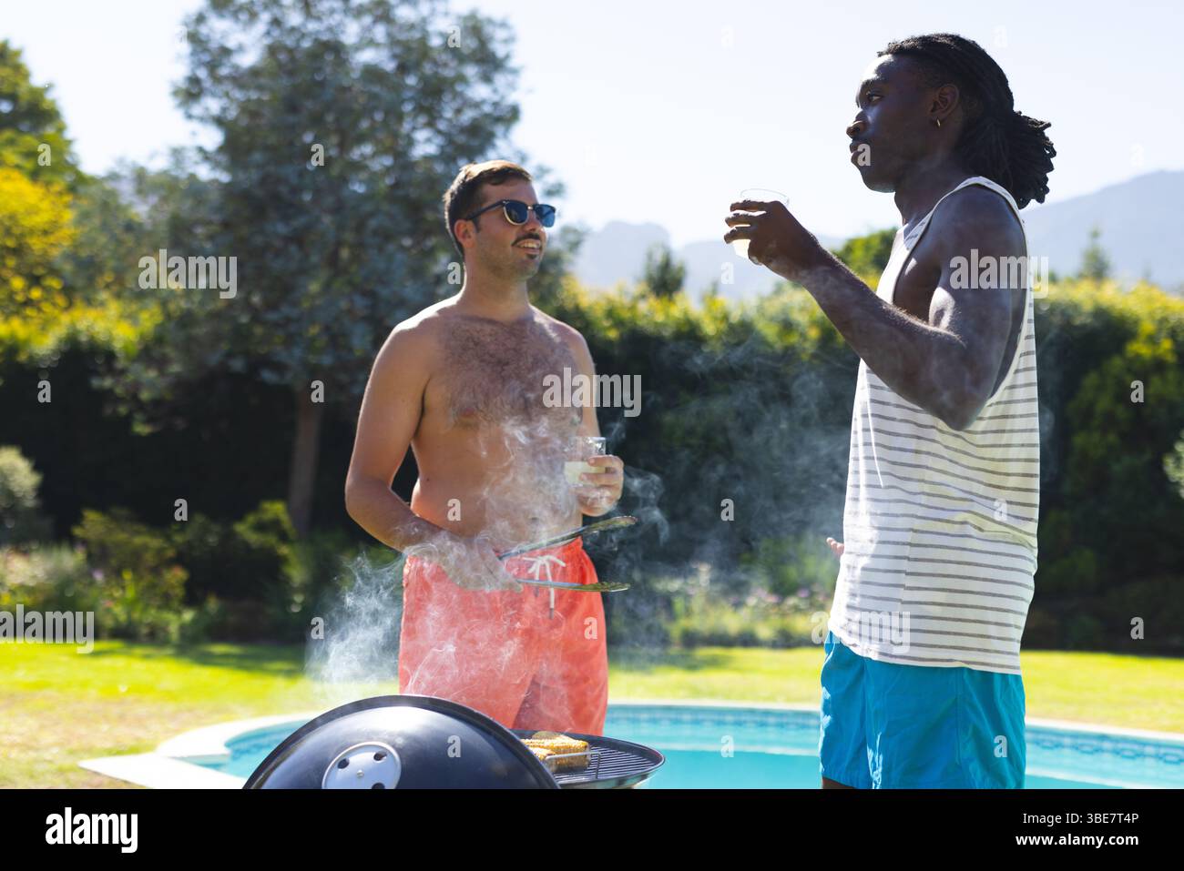 Diverse male friends grilling corn cobs on charcoal grill by swimming ...