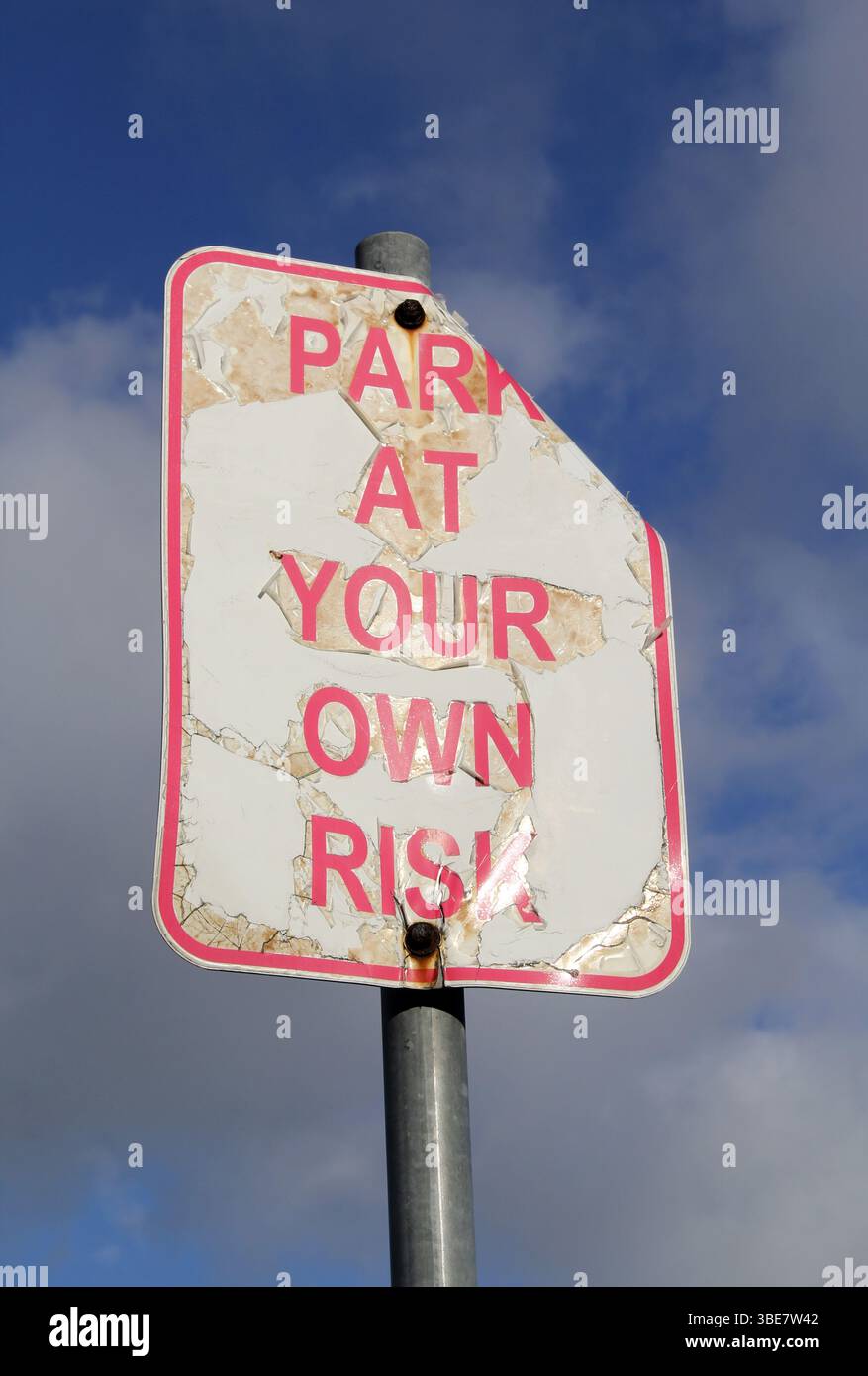 Damaged "Park At Your Own Risk" road sign against a blue sky with ...