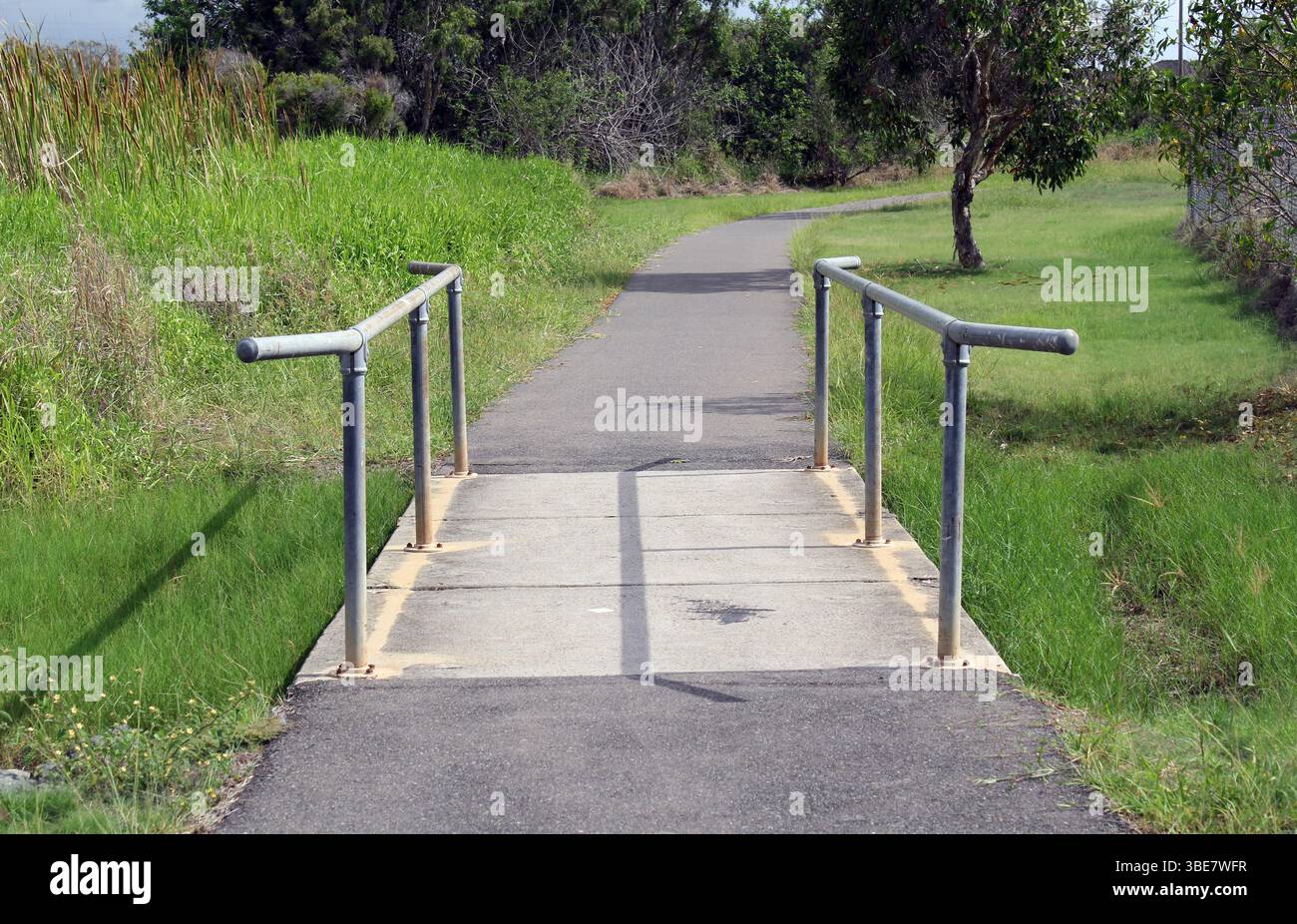 Bitumen asphalt bridge path with handrails surrounded by grass and ...
