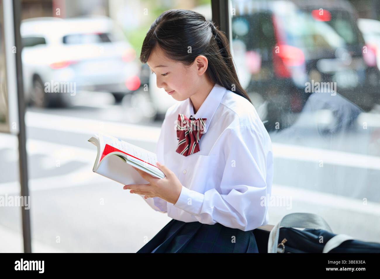 Junior high school girl reading reference book at bus stop Stock Photo ...