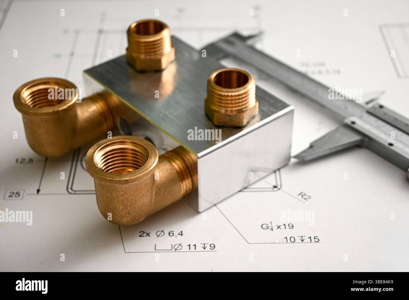 Plumbing manifold with brass fittings and caliper lying on a technical drawing or blueprint ...