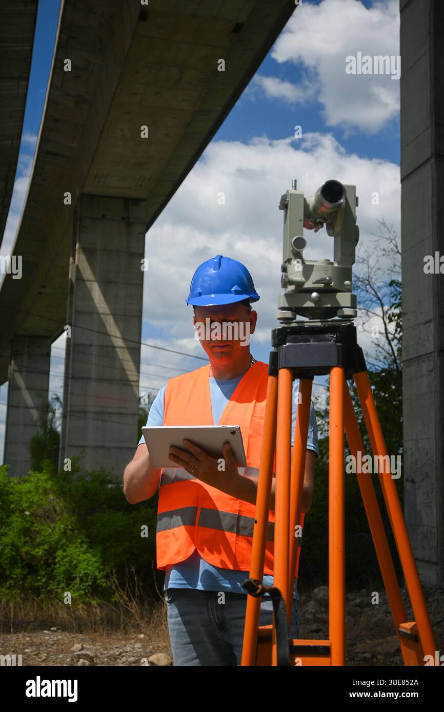Surveyor taking measurements with theodolite and digital tablet under a ...