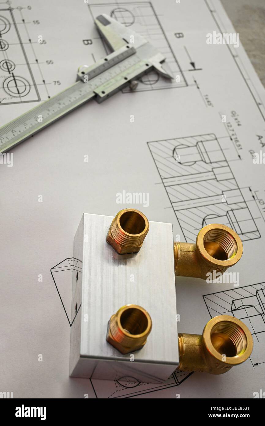 Metal plumbing fixture with brass connectors lying on blueprint ...