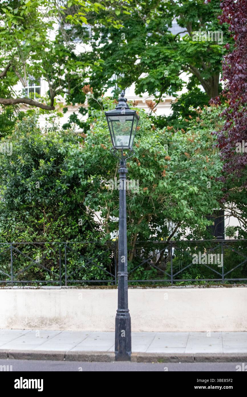 A traditional street lamp stands in front of lush bushes and trees in a ...