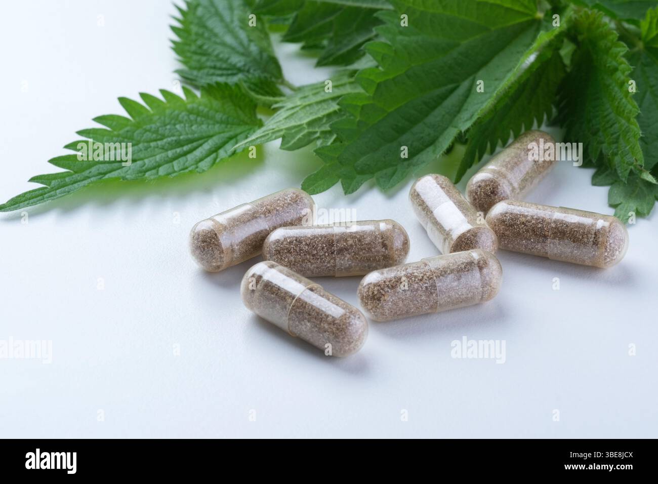 Herbal capsules displayed alongside vibrant green leaves on a clean ...