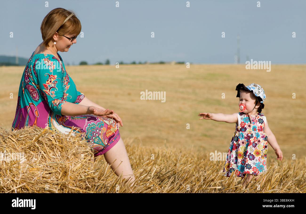 Happy mother and toddler girl playing in a summer field with haystacks ...