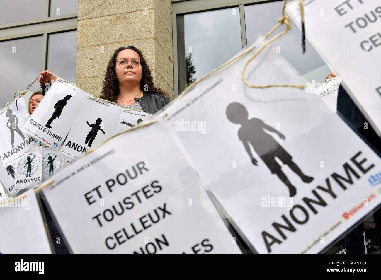 A woman peers behind a banner representing anonymous victims during a ...